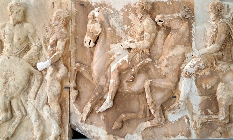 Close-up detail of ancient Greek marble relief carving showing horsemen