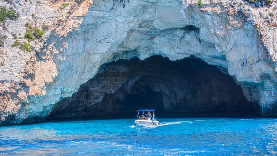 Boat approaching a blue-lit cave entrance against rocky cliffs