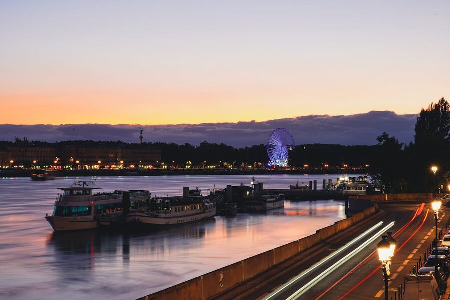Evening view of the Garonne River in Bordeaux with illuminated Ferris wheel and bridge reflections