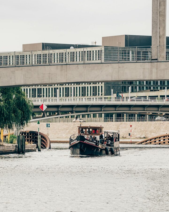 A tour boat navigating under a modern bridge on the Spree River in Berlin