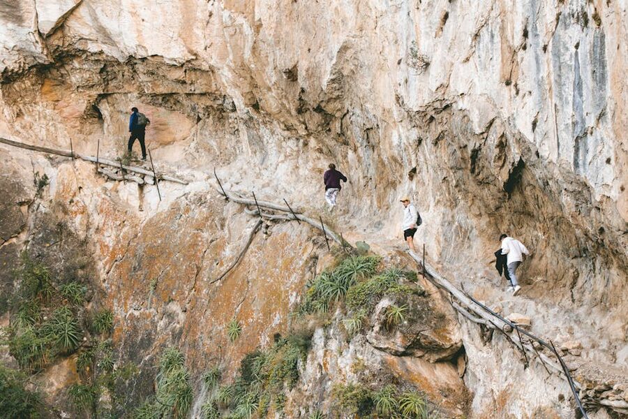 Narrow rocky path section of Caminito del Rey with hikers walking single file