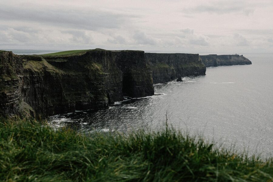 Cliffs of Moher rising above the Atlantic Ocean with green fields on top