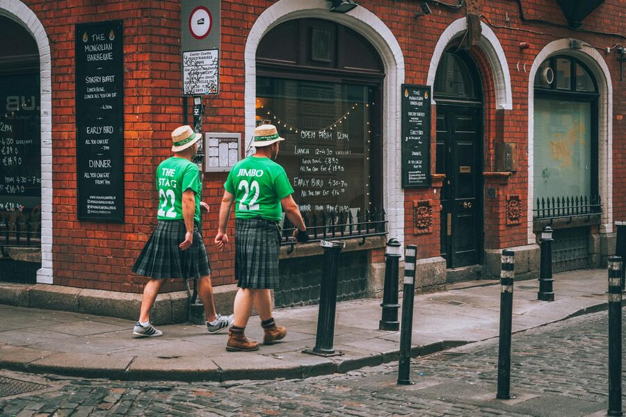 Two men in green jerseys and kilts walking past a restaurant in Dublin