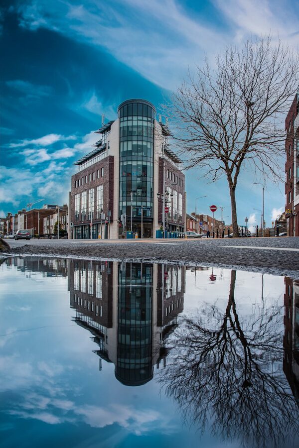 Modern Dublin building reflected in a puddle with clear sky