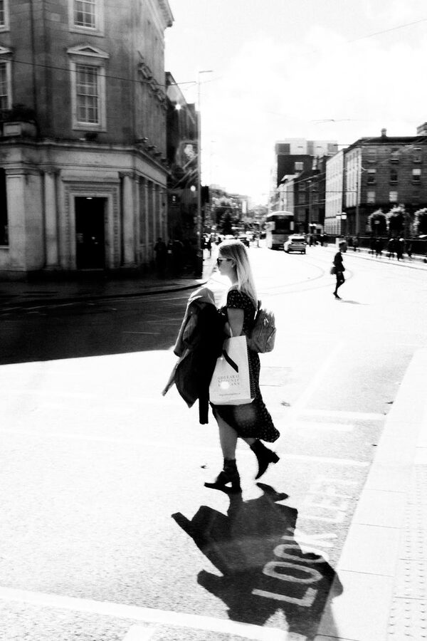 Woman crossing a sunlit Dublin street with dramatic shadows