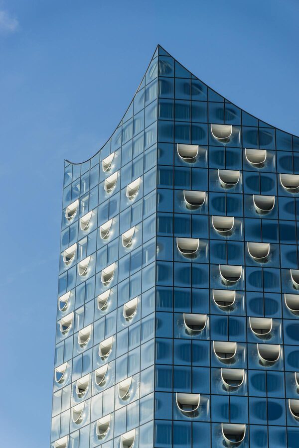Close-up of the Elbphilharmonie glass facade showing curved panels against blue sky