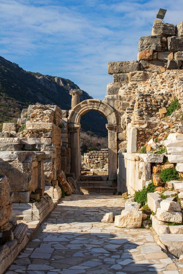 Stone archway among the Ephesus ruins with visitors walking through