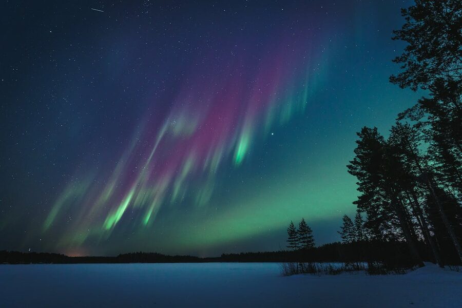 Northern Lights reflected in a calm Finnish lake surrounded by snow-covered trees