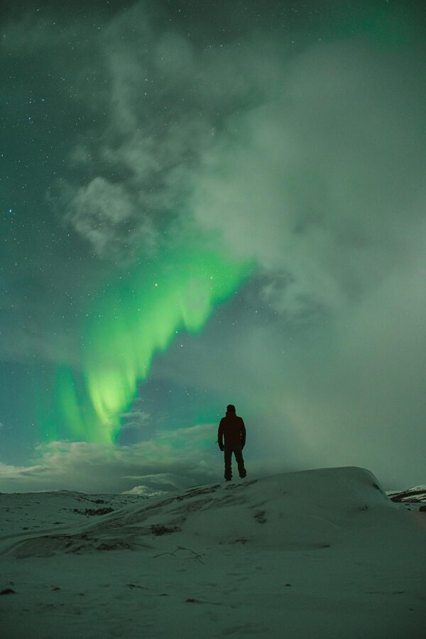 A person standing under bright green aurora borealis in a snowy field