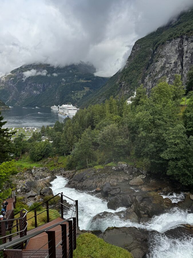 Cruise ship in a fjord with cascading waterfall and green mountains