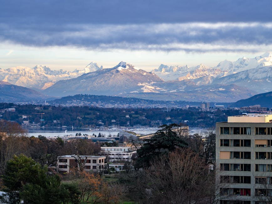 Geneva skyline with the Swiss Alps rising behind the city under a cloudy sky