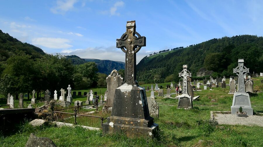 Celtic cross headstones in graveyard at Glendalough with green hills behind