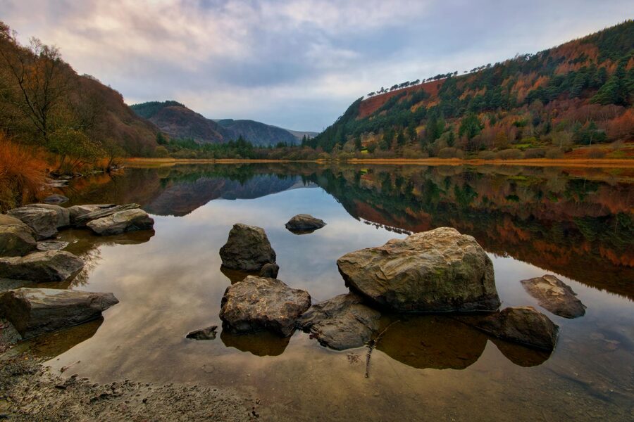 Glendalough lake at dawn with autumn foliage reflected in still water