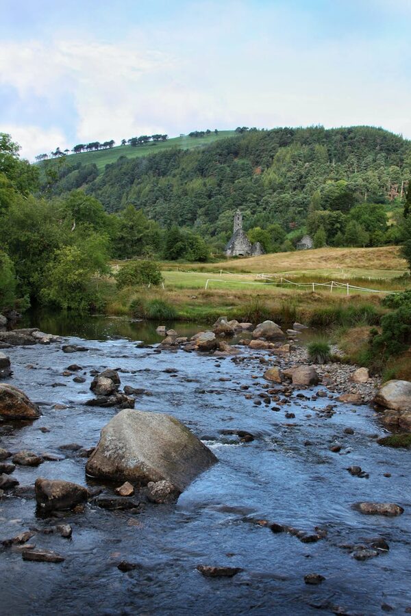 River flowing through green valley with medieval ruins at Glendalough