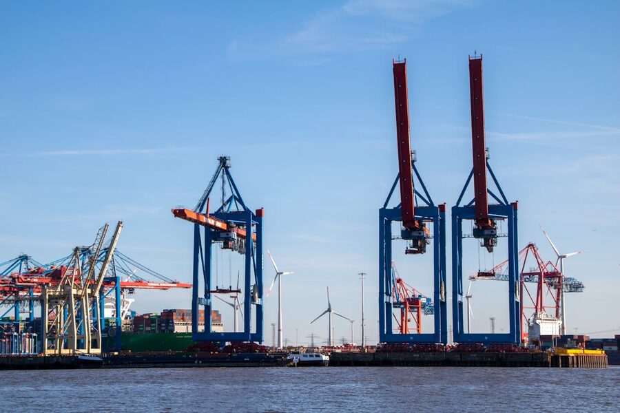 Cranes at Hamburg harbor with blue skies and wind turbines