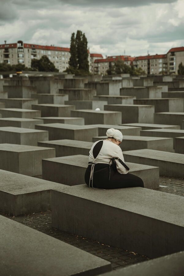 Person sitting alone among the concrete blocks of Berlin's Holocaust Memorial in reflection