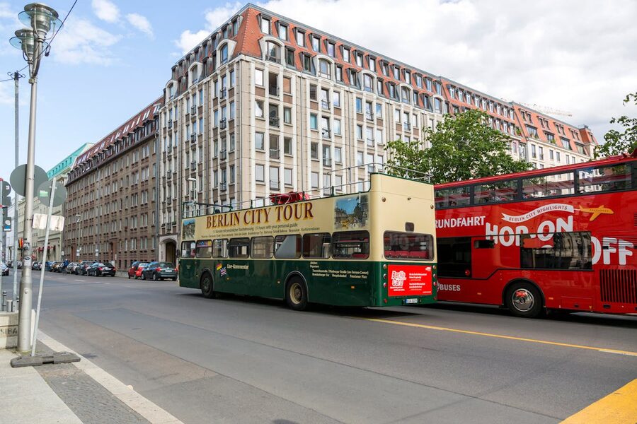 Double-decker tour buses driving through a Berlin street on a sunny day