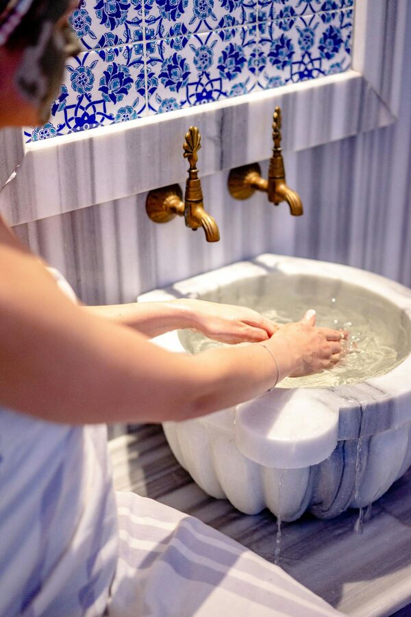 Ornate marble basin with decorative tiles and brass faucets in a Turkish hammam