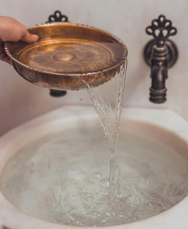 Hand pouring water from a decorative bowl in a Turkish bath setting