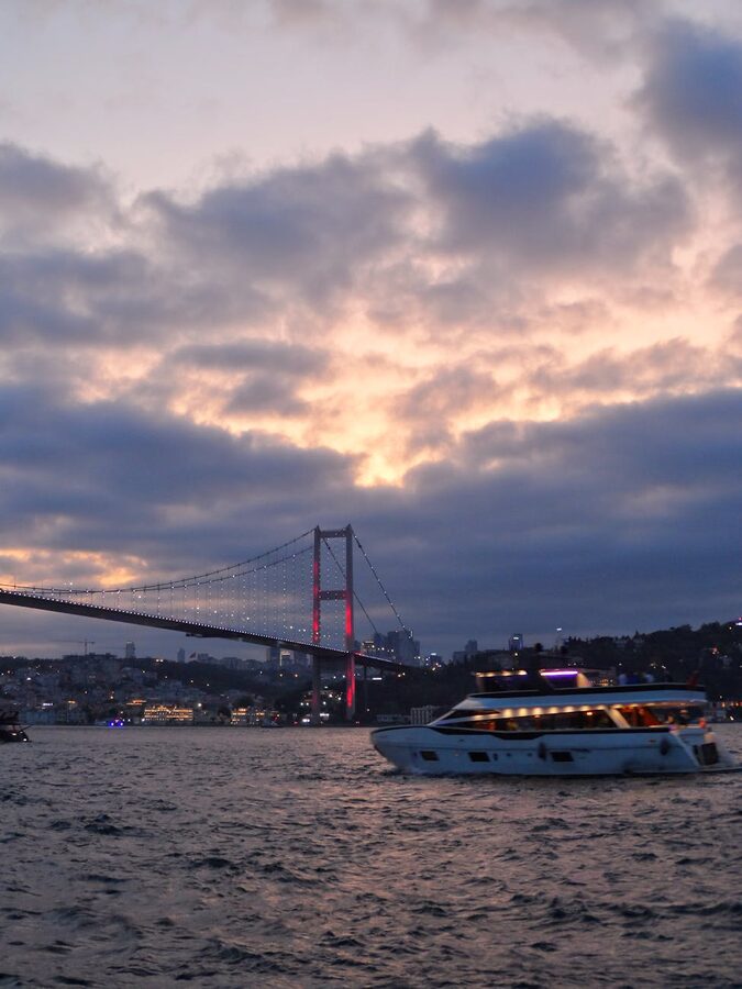 Boat cruising on the Bosphorus at sunset with bridge illuminated