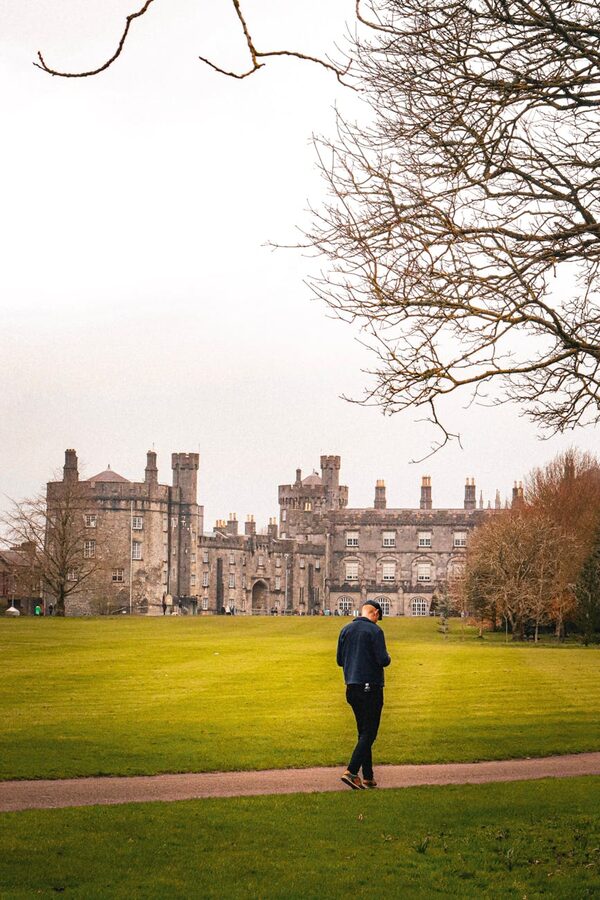 Person walking on path toward Kilkenny Castle on a cloudy day