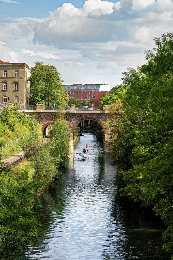 Small boats on a green canal under a stone bridge in Leipzig Germany