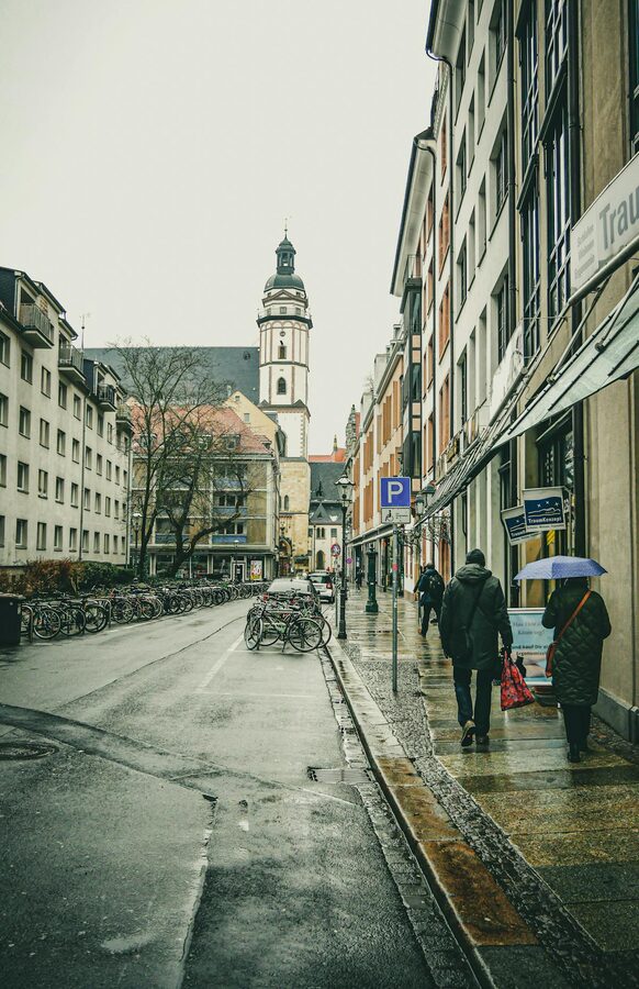 Rainy day on a Leipzig street with church and pedestrians with umbrellas