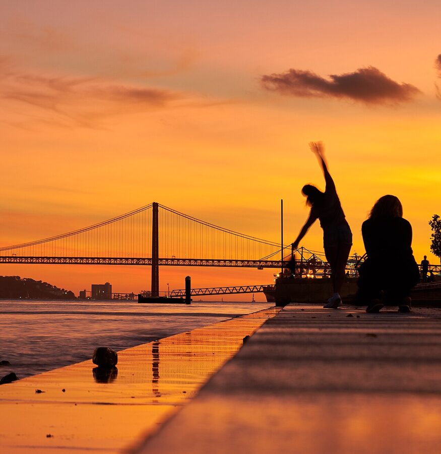 People silhouetted against the 25 de Abril Bridge in Lisbon at sunset