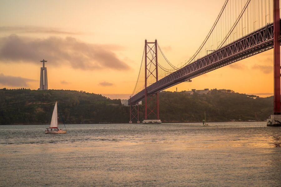 Small sailboat against the 25 de Abril Bridge at sunset Lisbon