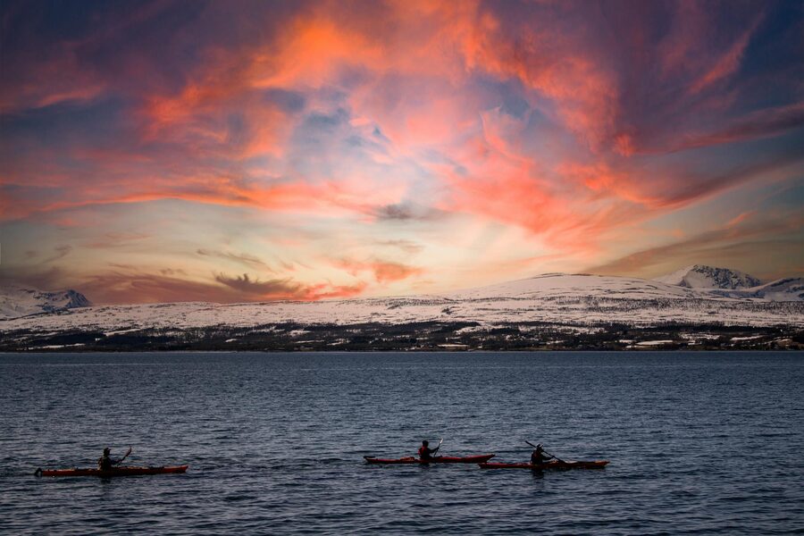 Kayakers paddling at sunset with snow-covered mountains in background