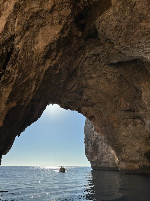 A boat passing through sea caves in Malta with blue light reflecting off the water
