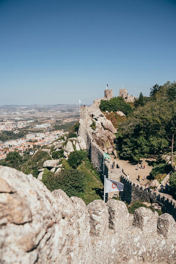 Medieval stone fortress wall climbing a green hillside in Sintra