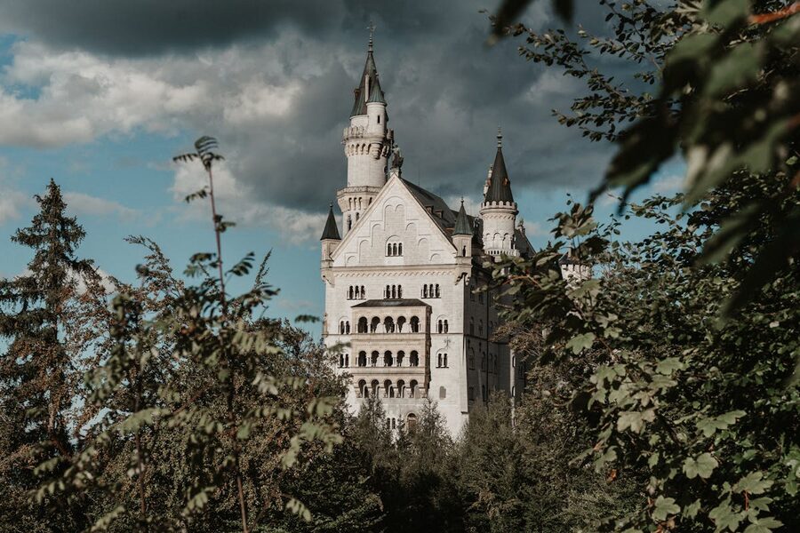 Neuschwanstein Castle framed by lush forest and trees under dramatic sky in Bavaria