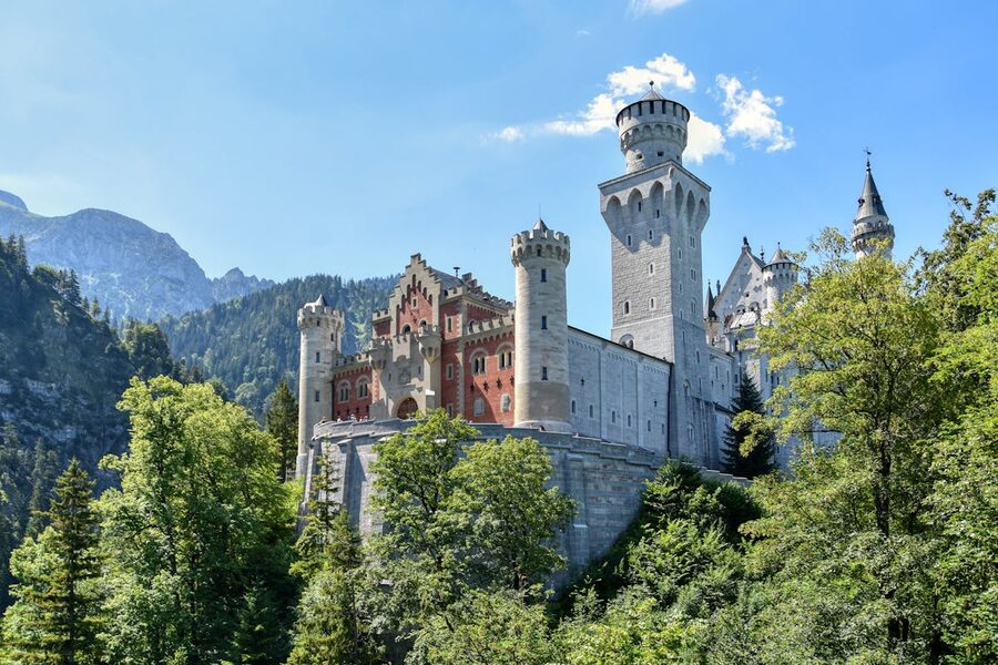 Neuschwanstein Castle surrounded by lush greenery and blue skies in summer