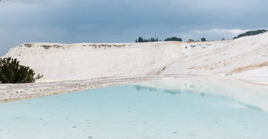 Azure thermal pools on white travertine terraces at Pamukkale under cloudy sky