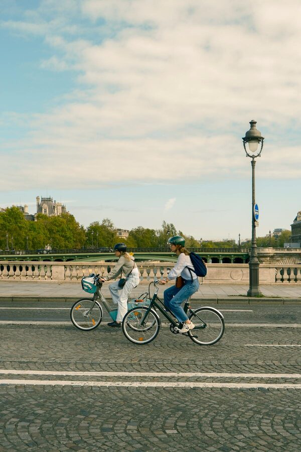 Two cyclists riding along a Paris street with classic Haussmann buildings in the background