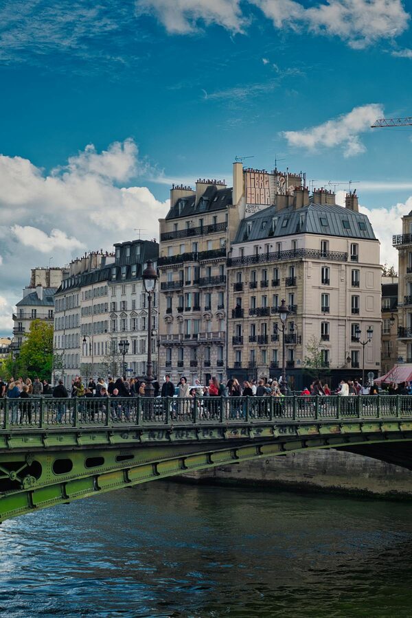 People crossing a Paris bridge with classic Haussmann buildings behind