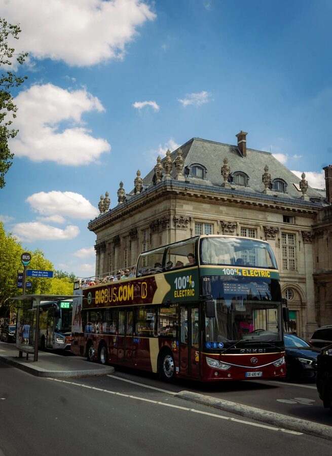 A double-decker electric bus in front of Parisian architecture