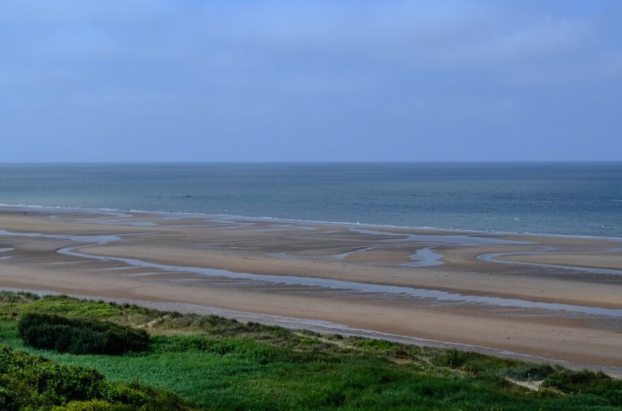 Wide view of Omaha Beach in Normandy with calm sea and vast sand under open sky