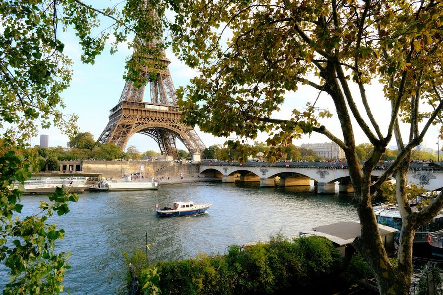The Eiffel Tower from across the Seine River with green trees along the bank