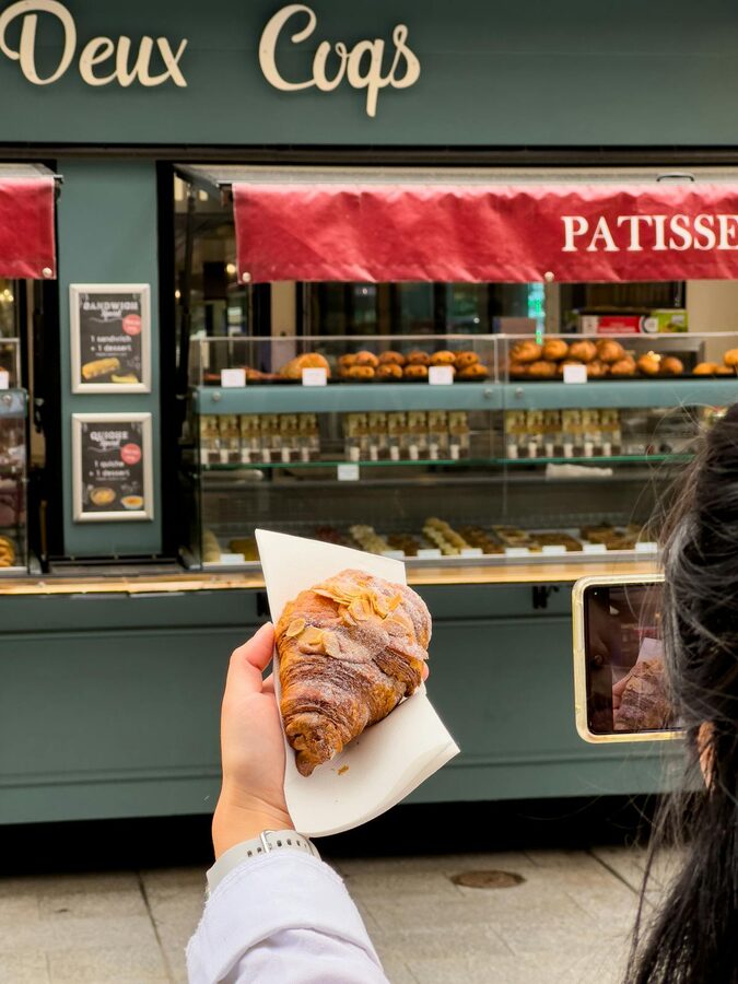 Person holding a croissant outside a Parisian patisserie