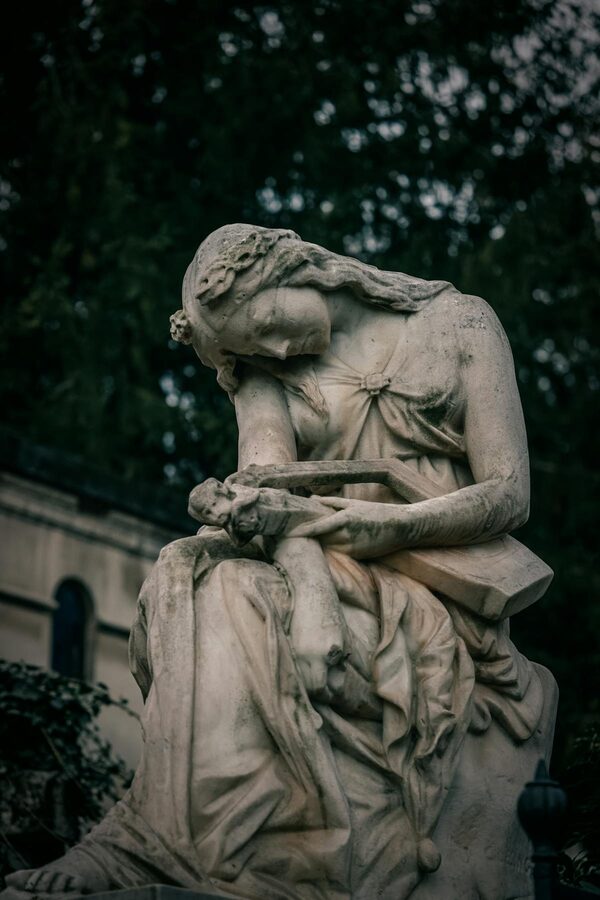 Melancholic marble statue in a Paris cemetery surrounded by trees