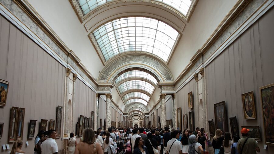Visitors walking through a corridor of paintings inside the Louvre Museum