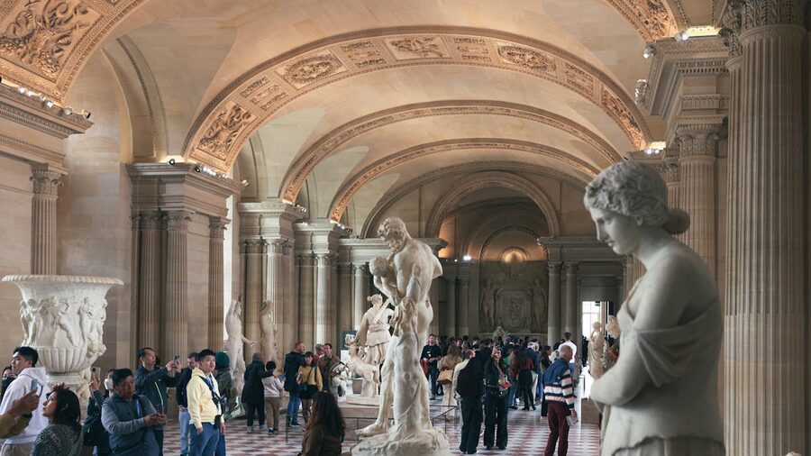 Crowded hall in the Louvre Museum with classical statues and visitors