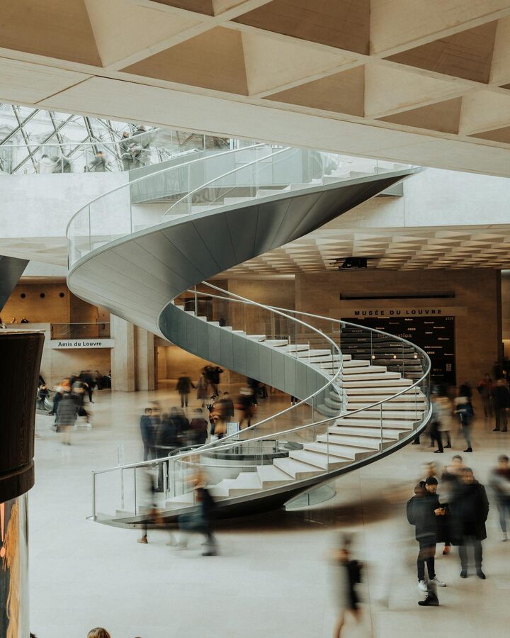Visitors on the modern spiral staircase in the Louvre Museum main hall
