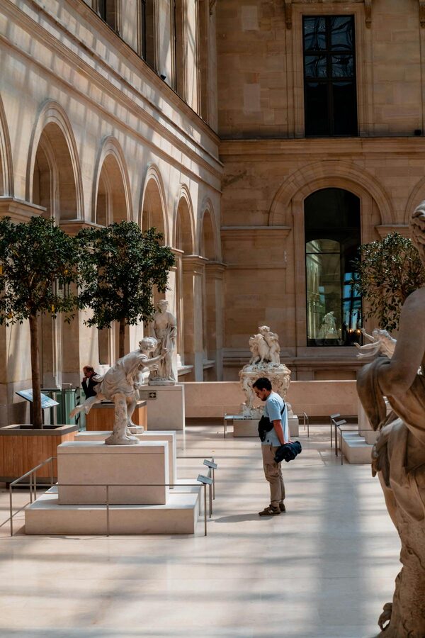A visitor admiring sculptures inside the Louvre Museum in Paris