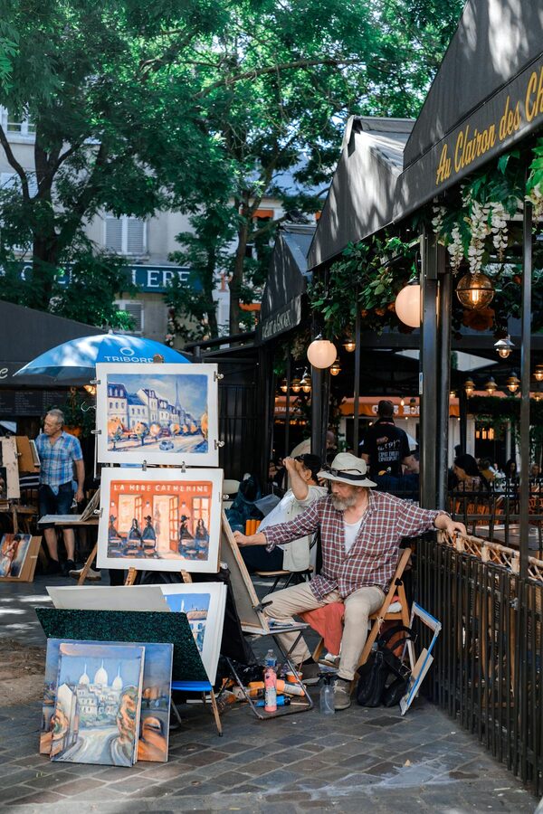 Street artist painting scenic views at an easel in Montmartre with displayed artworks