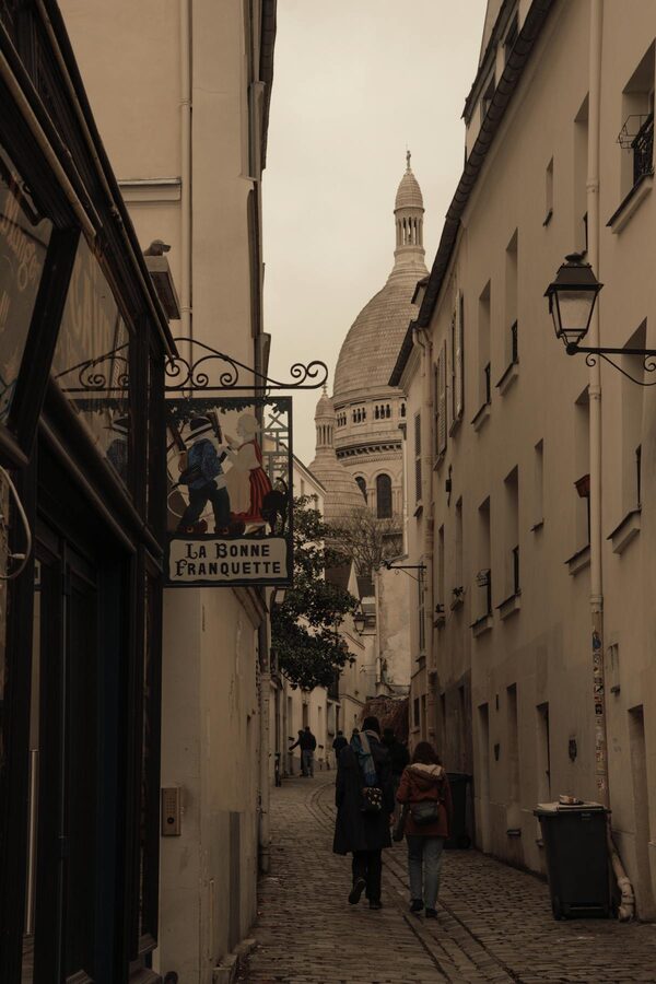 Narrow lane in Montmartre with the Sacré-Coeur dome visible between the buildings