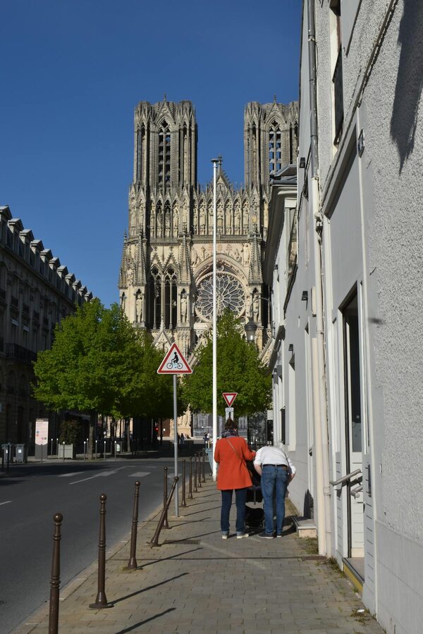 Street-level view of Reims Cathedral with pedestrians walking nearby