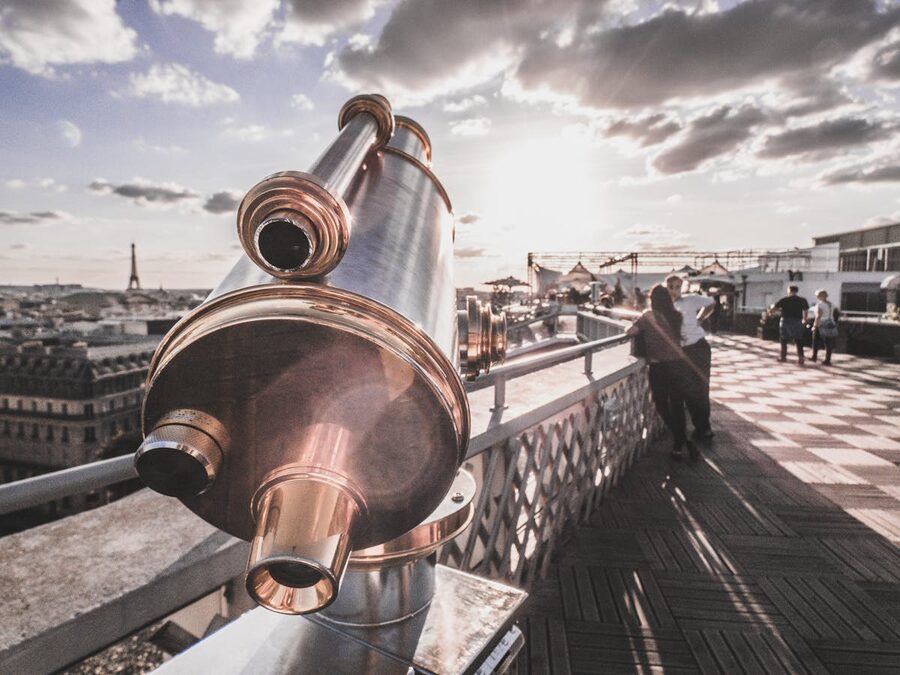 Coin-operated telescope on observation deck with Paris skyline and Eiffel Tower behind it